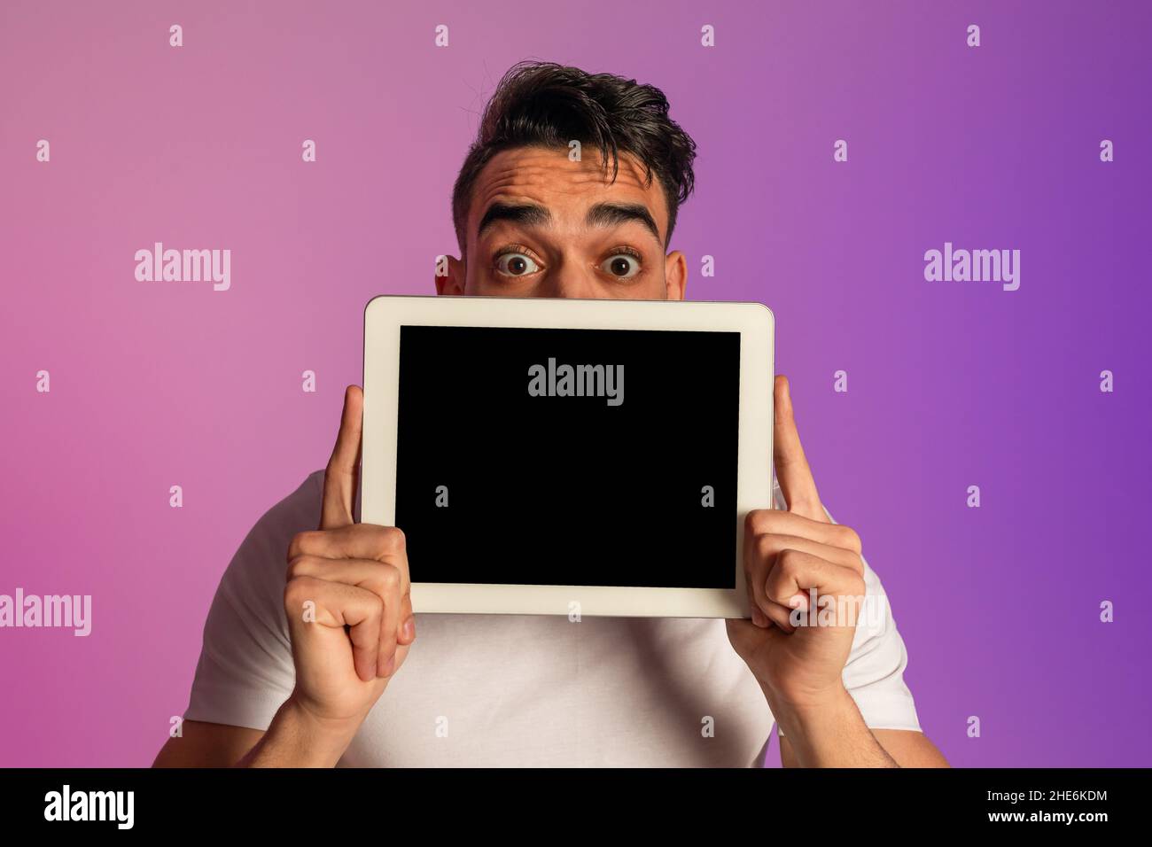Shocked millennial Arab man hiding behind tablet with blank screen in ...