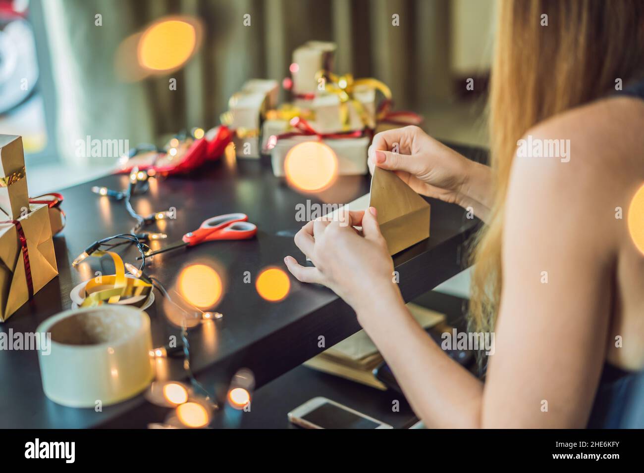 Young woman is packing presents. Present wrapped in craft paper with a ...