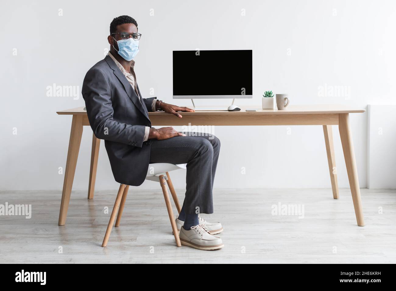 Black manager in anti covid face mask sitting at desk in home office ...