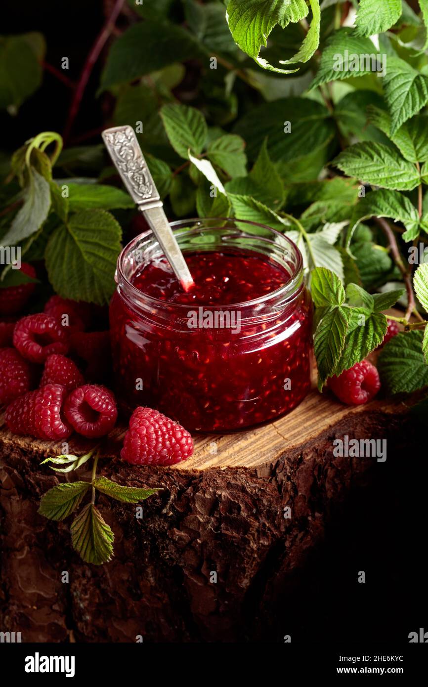 Jar of raspberry jam and fresh berries with leaves on a pine stump in ...