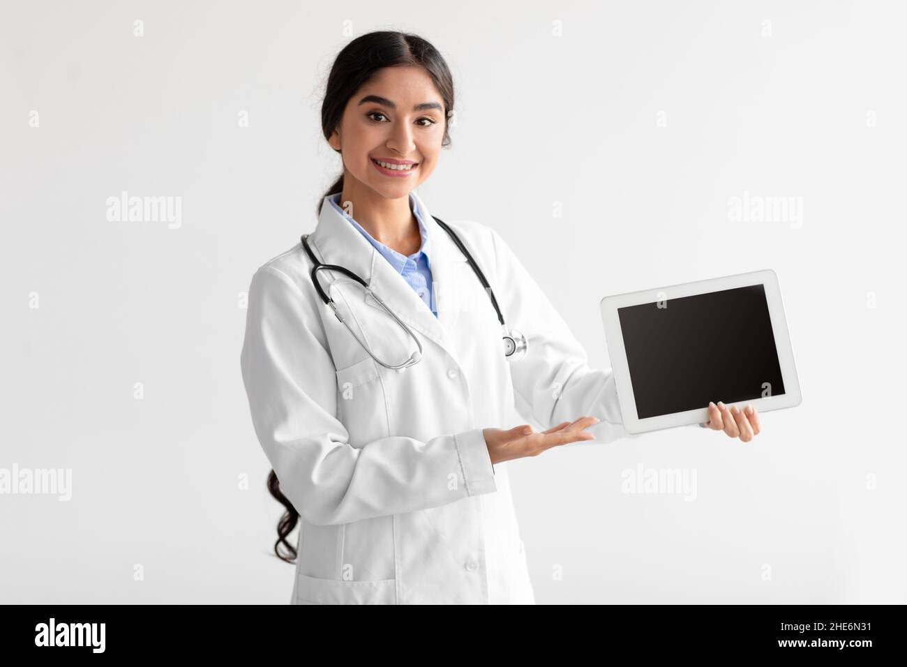 Satisfied young cute indian woman nurse in uniform shows digital tablet ...
