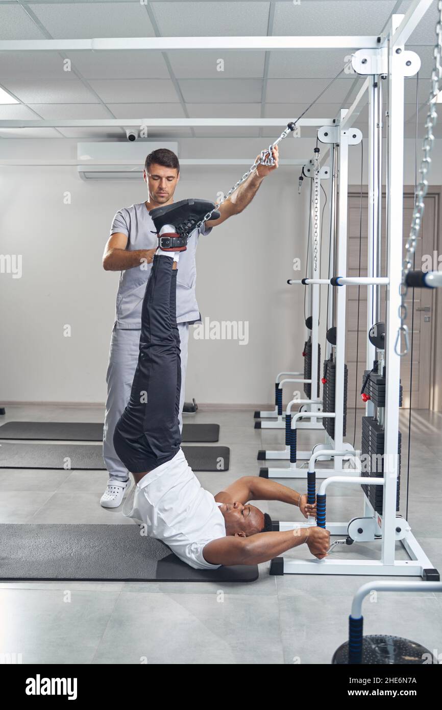 Male patient working out at gym with professional physiotherapist Stock ...