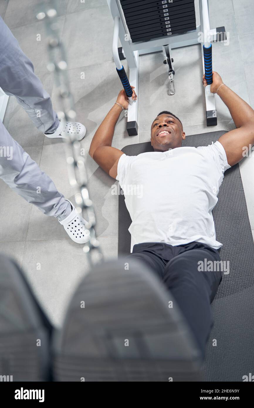Joyous male patient performing exercise using gym equipment Stock Photo ...