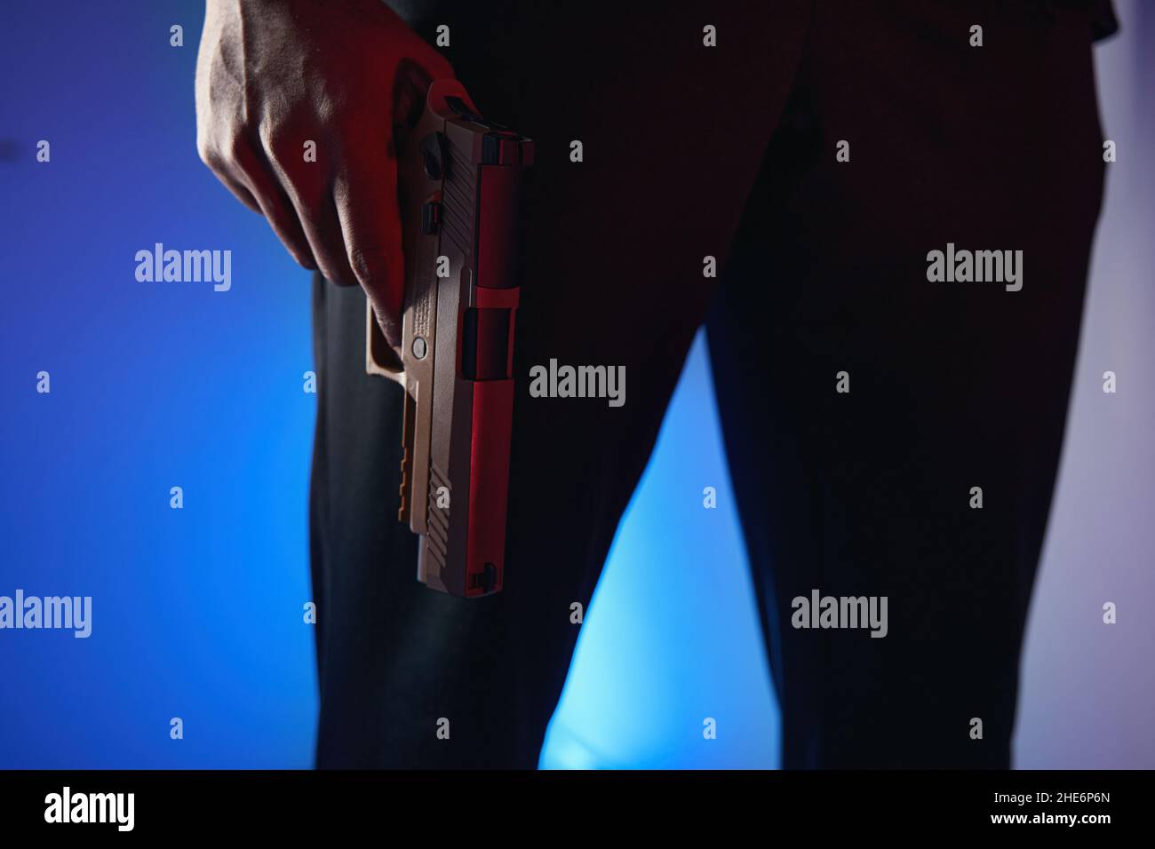 Person holding pistol near his legs indoors Stock Photo - Alamy