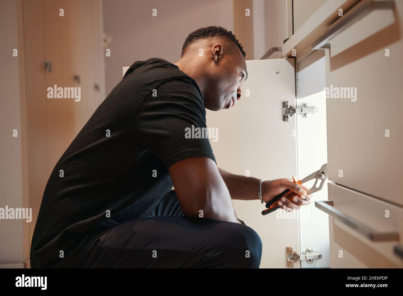 Man using pliers to repair cupboard drawer in kitchen Stock Photo - Alamy