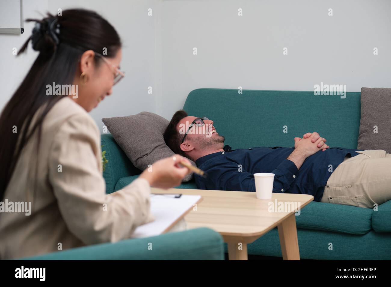 Asian female psychologist and caucasian man patient laughing at therapy ...