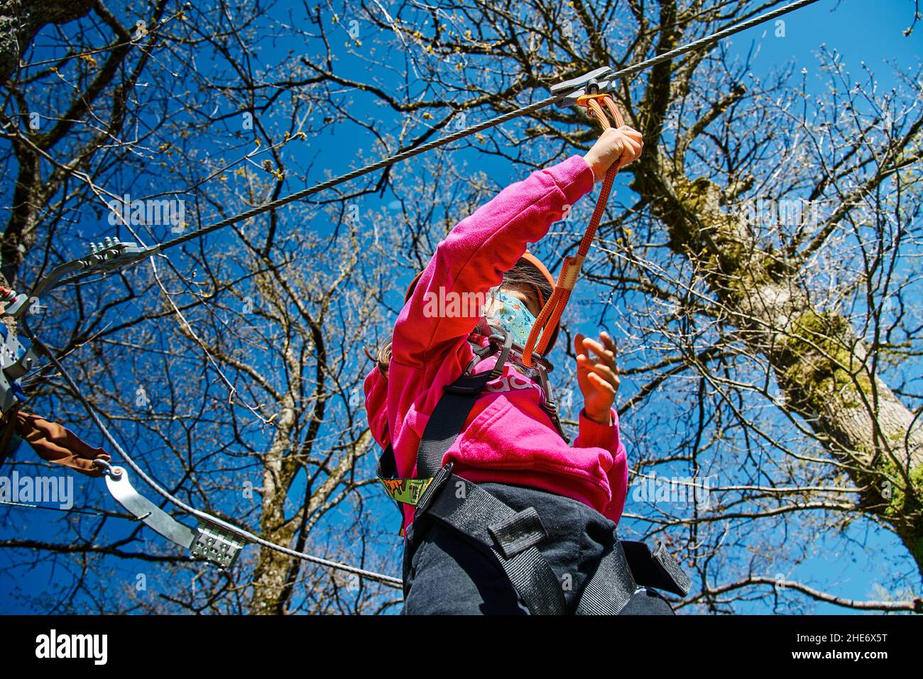 Little girl with protections practicing climbing between trees with ...