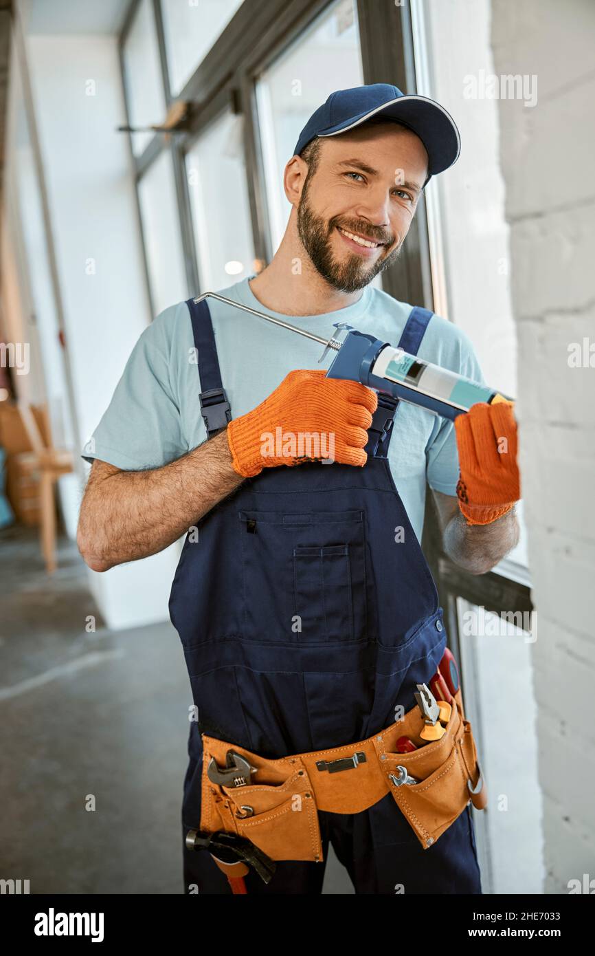 Cheerful man fixing window with silicone adhesive gun Stock Photo - Alamy