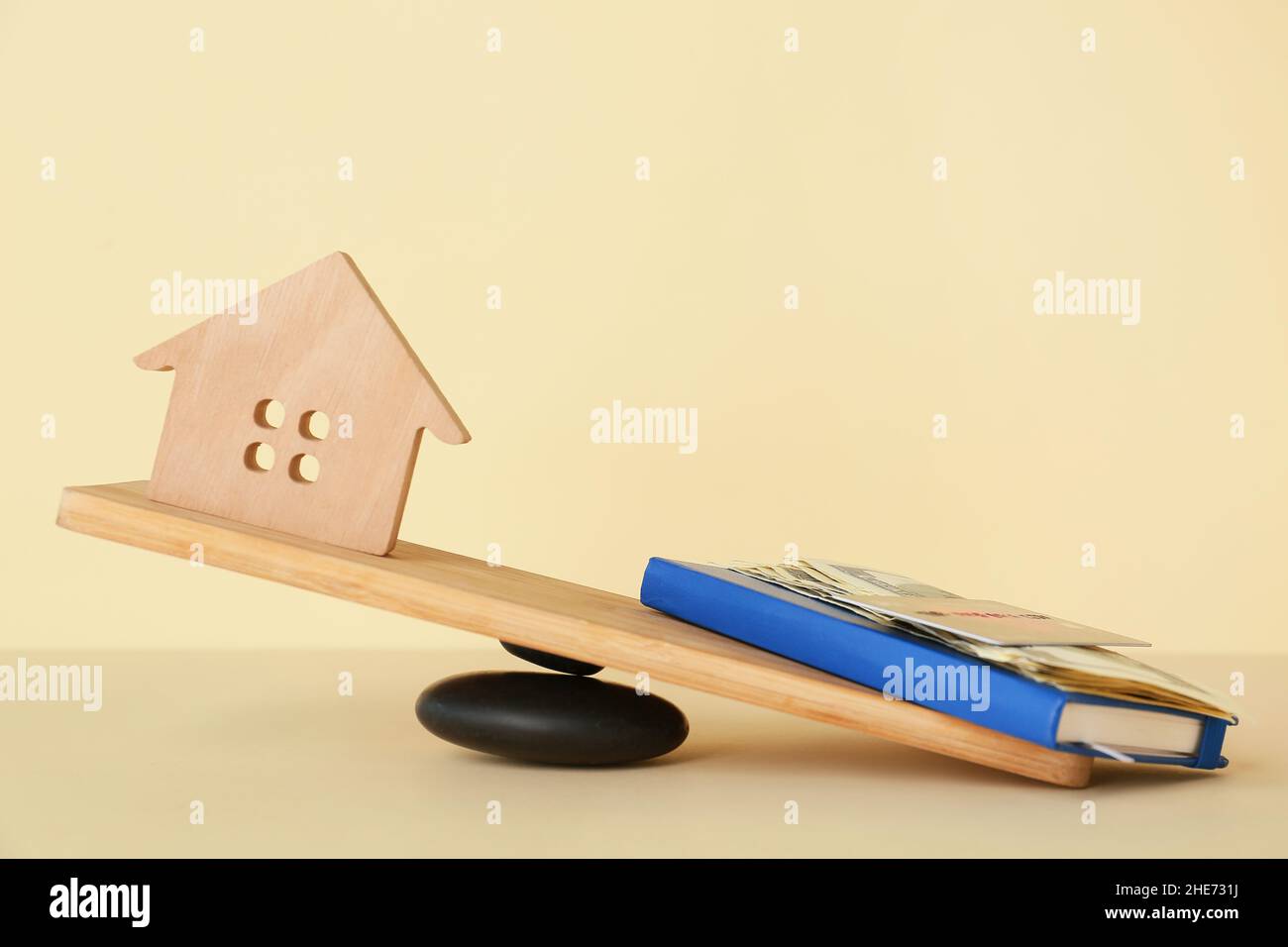 Model of house and notebook with money on teeterboard against light ...