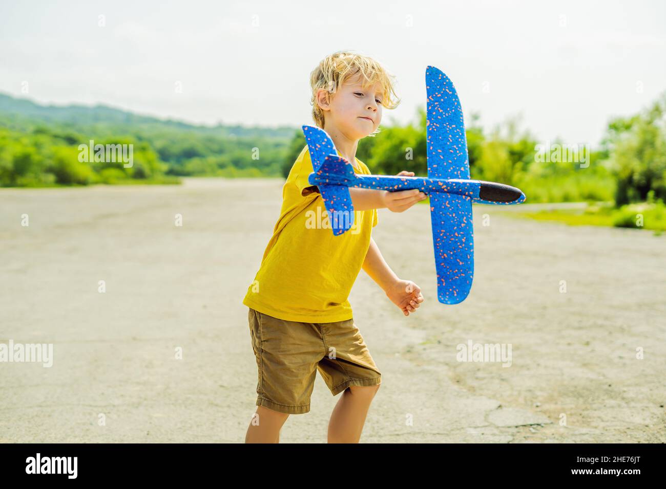 Happy kid playing with toy airplane against old runway background ...
