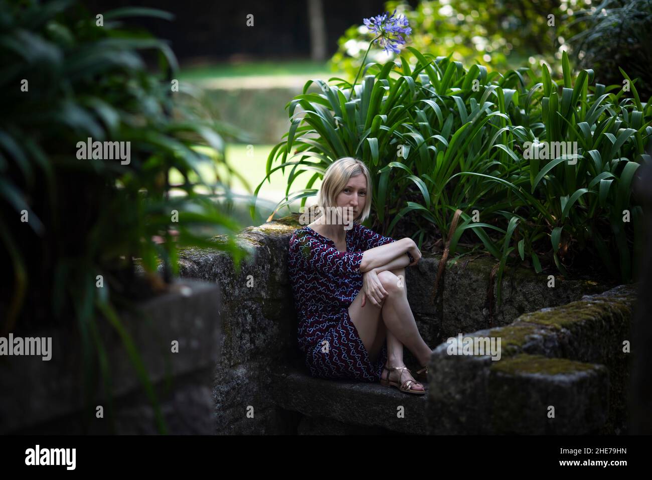 A young woman sitting on a stone bench in an ancient Portuguese park ...