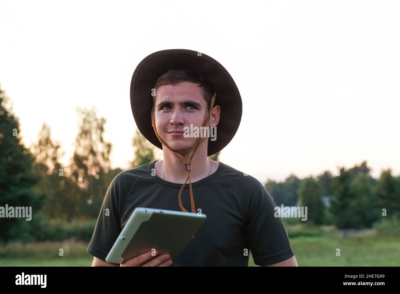 Young man farmer in cowboy hat at agricultural field on sunset holding ...