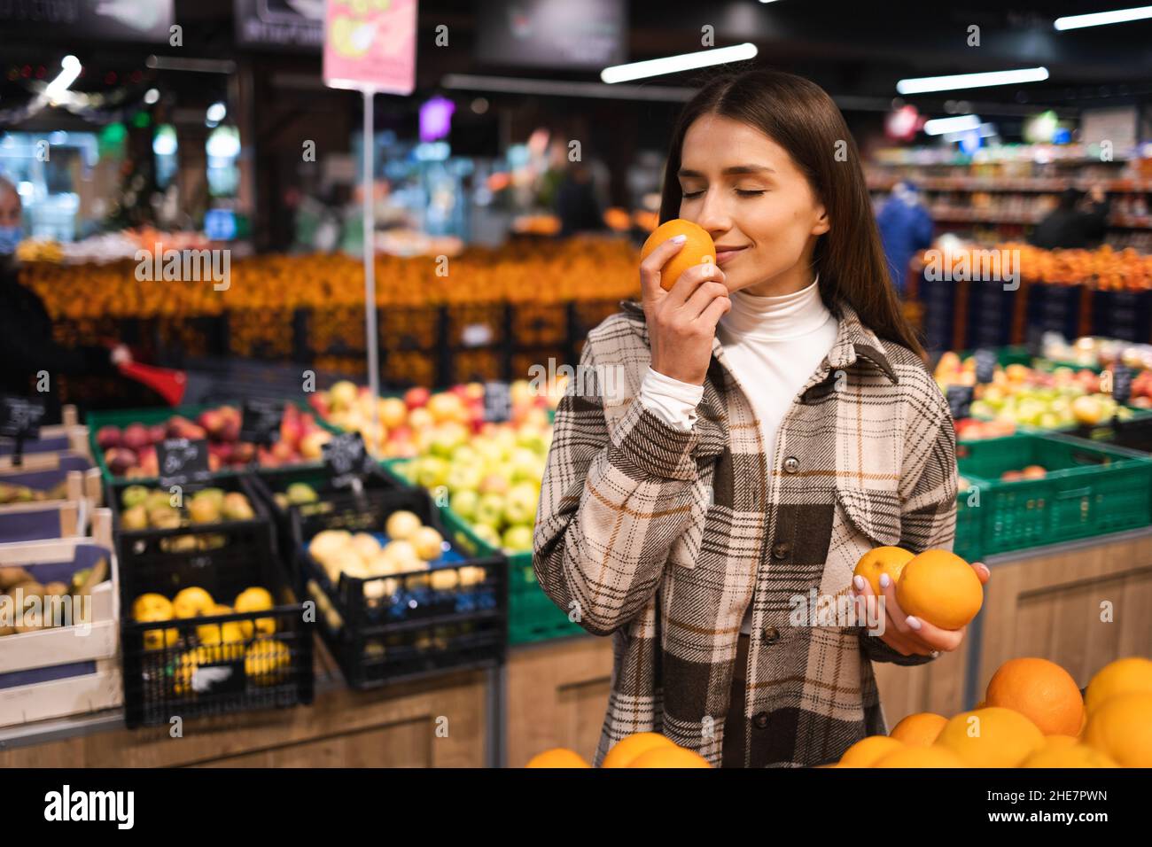 Female customer smelling orange in a supermarket. Woman chooses oranges ...