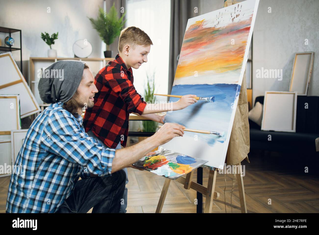 Qualified male teacher drawing with little boy on canvas using colorful ...