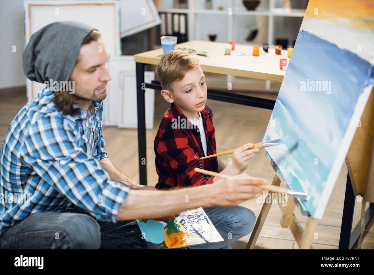 Caucasian male tutor showing all details of art painting to cute boy ...