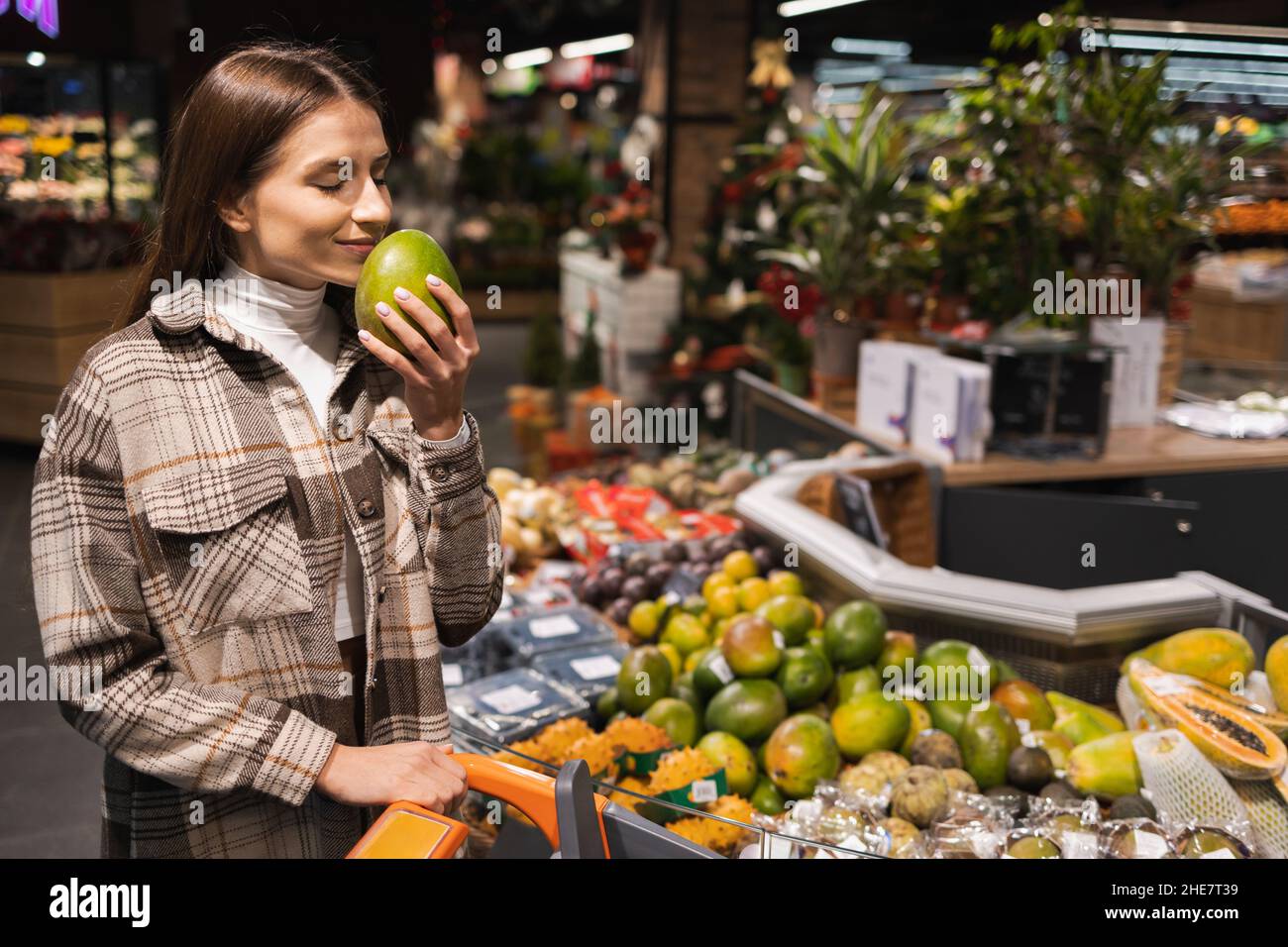 Female customer in supermarket smelling mango. Woman chooses fruit in ...