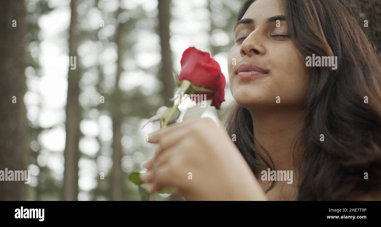 Beautiful Indian woman smelling a fresh red rose at park Stock Photo ...