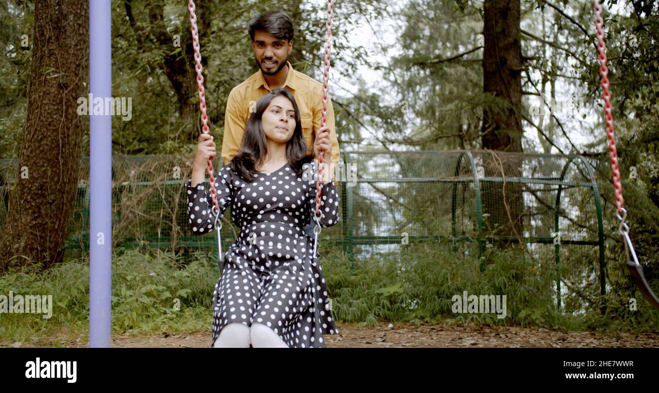 Young Indian man pushing his girlfriend on a swing - a date at a park ...