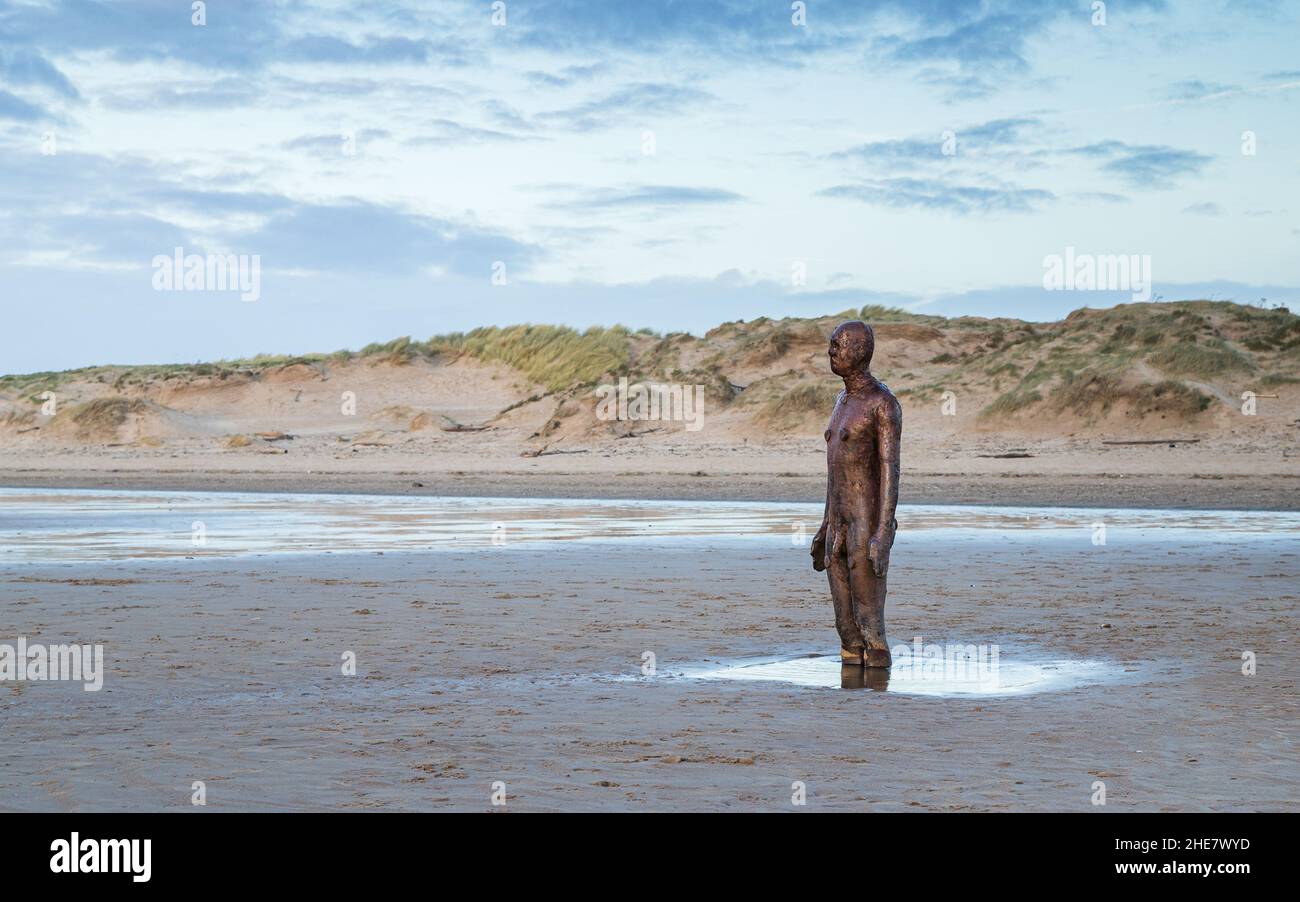 A lone Iron Man on Crosby beach seen in front of the sand dunes on the ...