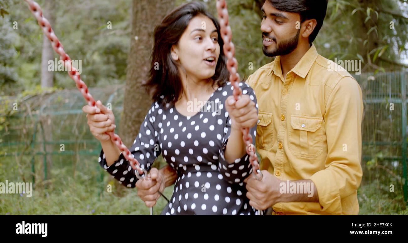 Young Indian man pushing hi girlfriend on a swing - a date at a park ...