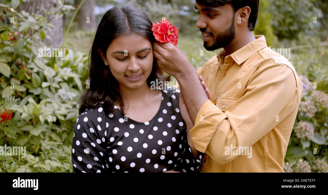 Young Indian man, putting a red flower on the ear of his girlfriend at ...