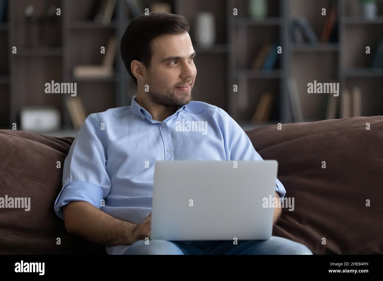 Dreamy man distracted from laptop using, sitting on couch Stock Photo - Alamy