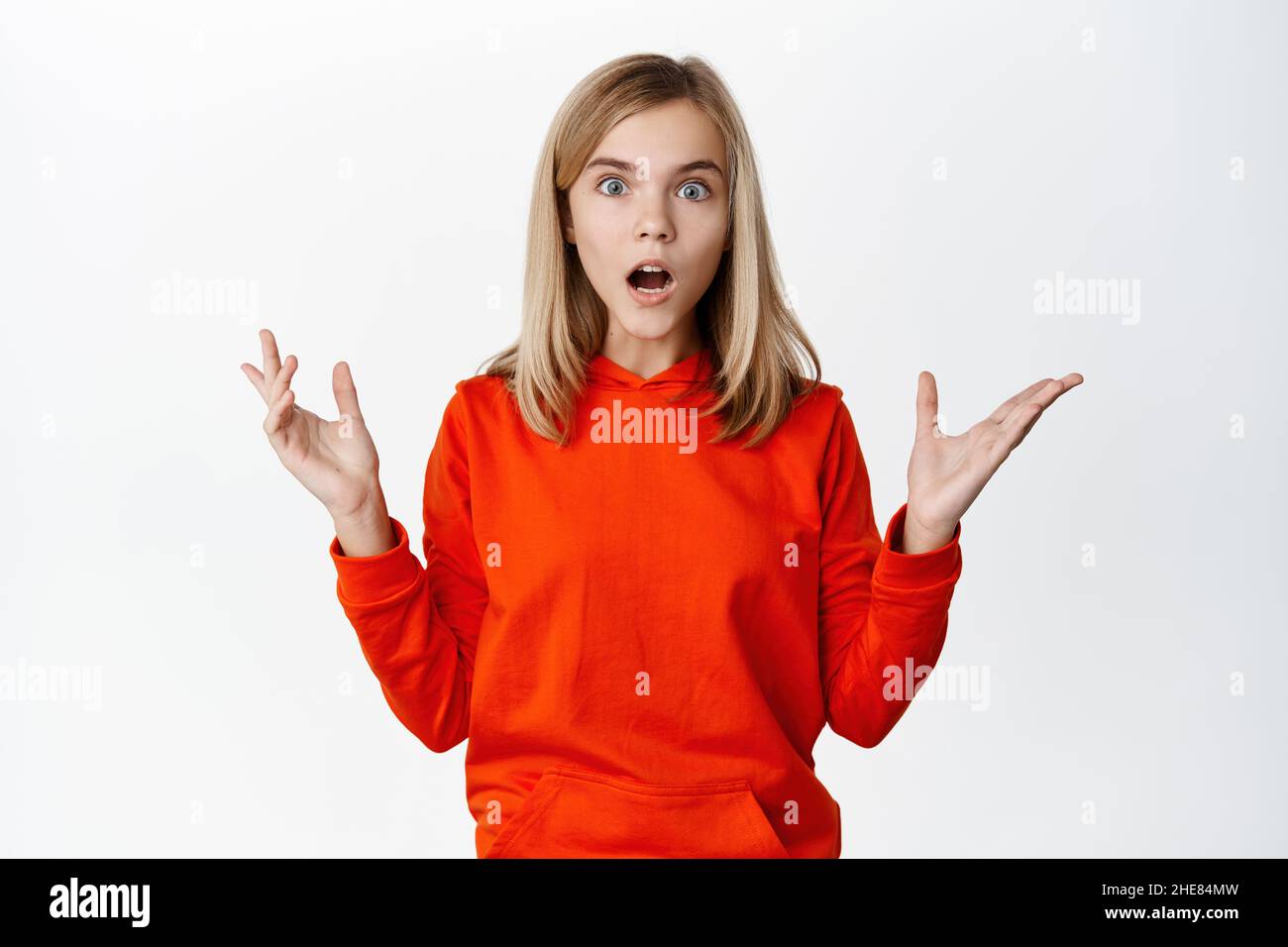 Surprised and shocked little blond girl looks down startled, seeing ...