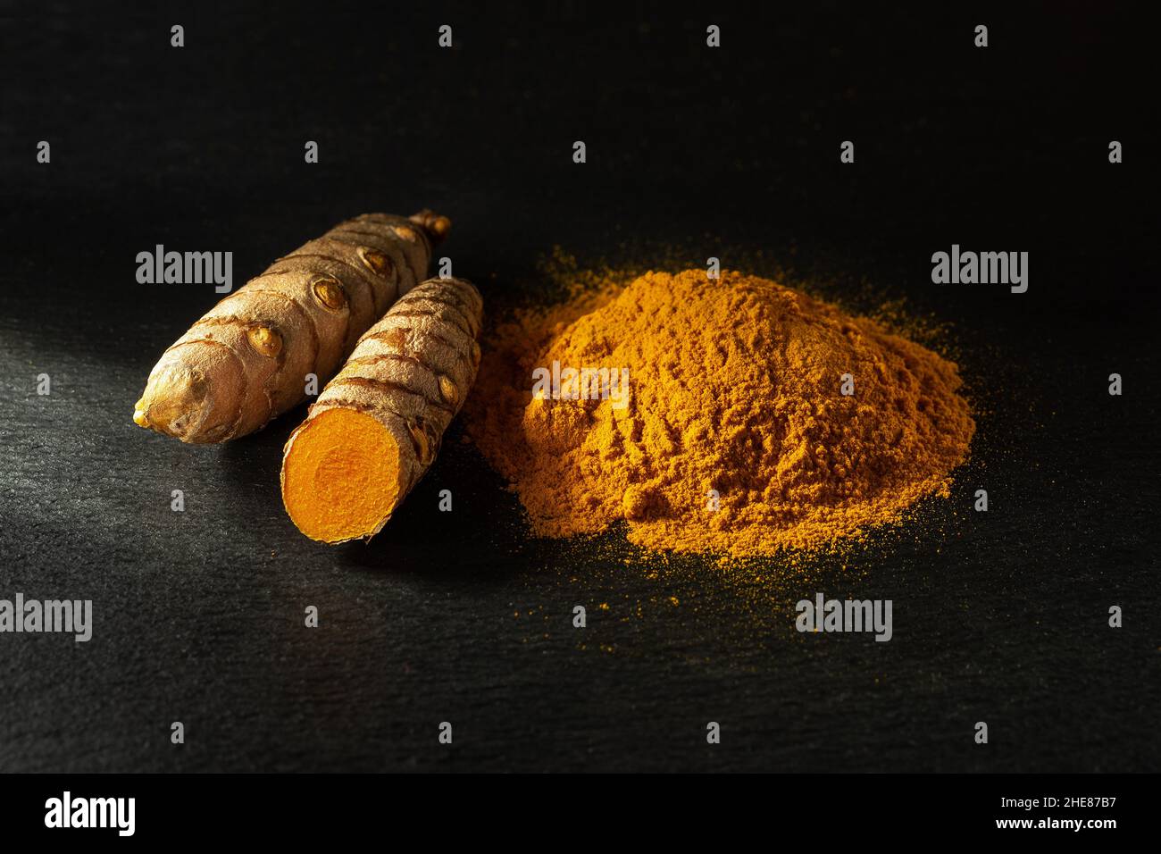 Raw whole turmeric roots and organic curcuma powder on a black slate ...