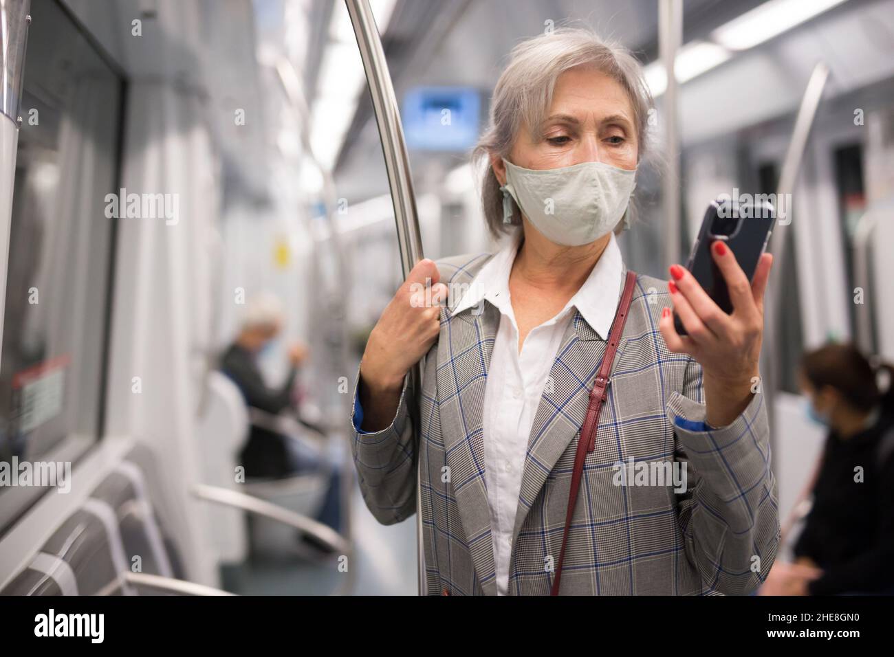 Senior lady in mask standing in metro train and using smartphone Stock ...