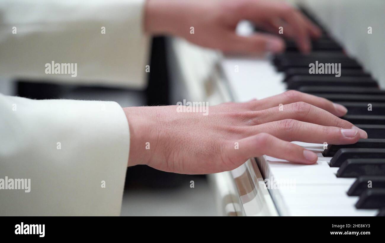 Close-up hands of a young man in a white jacket play music on the piano ...