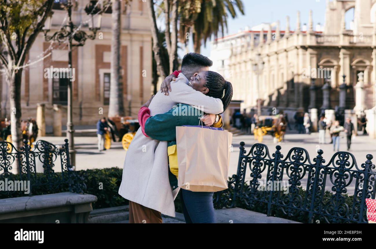 Man and woman hugging while holding bags with presents outdoors Stock ...