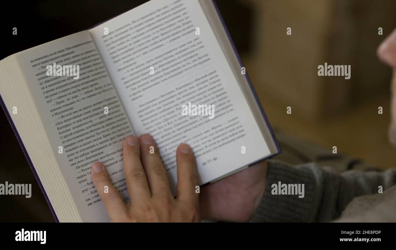 Over the shoulder view of a man reading a book at home. Middle aged ...