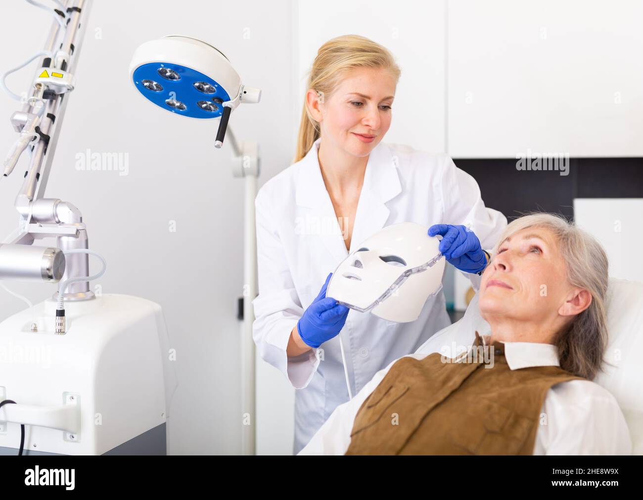 Cosmetologist putting spectrum mask on senior woman's face Stock Photo ...