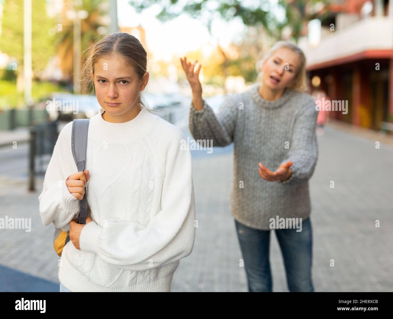 Upset teen girl walking on city street with worried mother reproaching ...