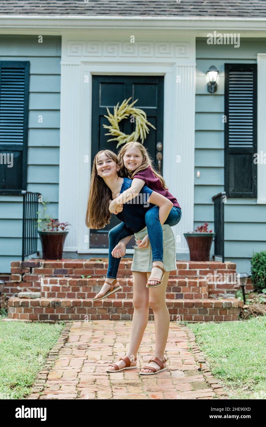An older sister holding her 10 year old sister piggyback on her back ...