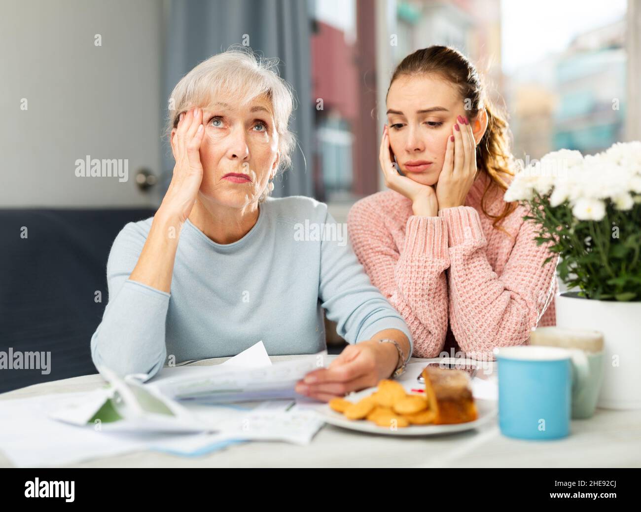Upset young woman with aged mother looking worriedly at papers at home ...