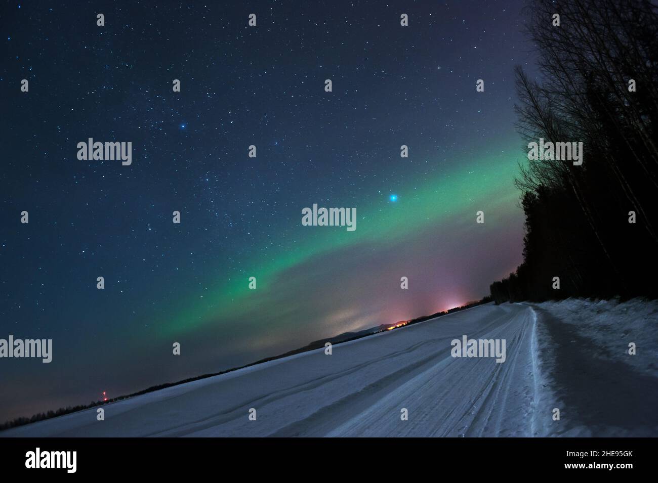 Snowy road leading through winter landscape. Stars and northern lights ...