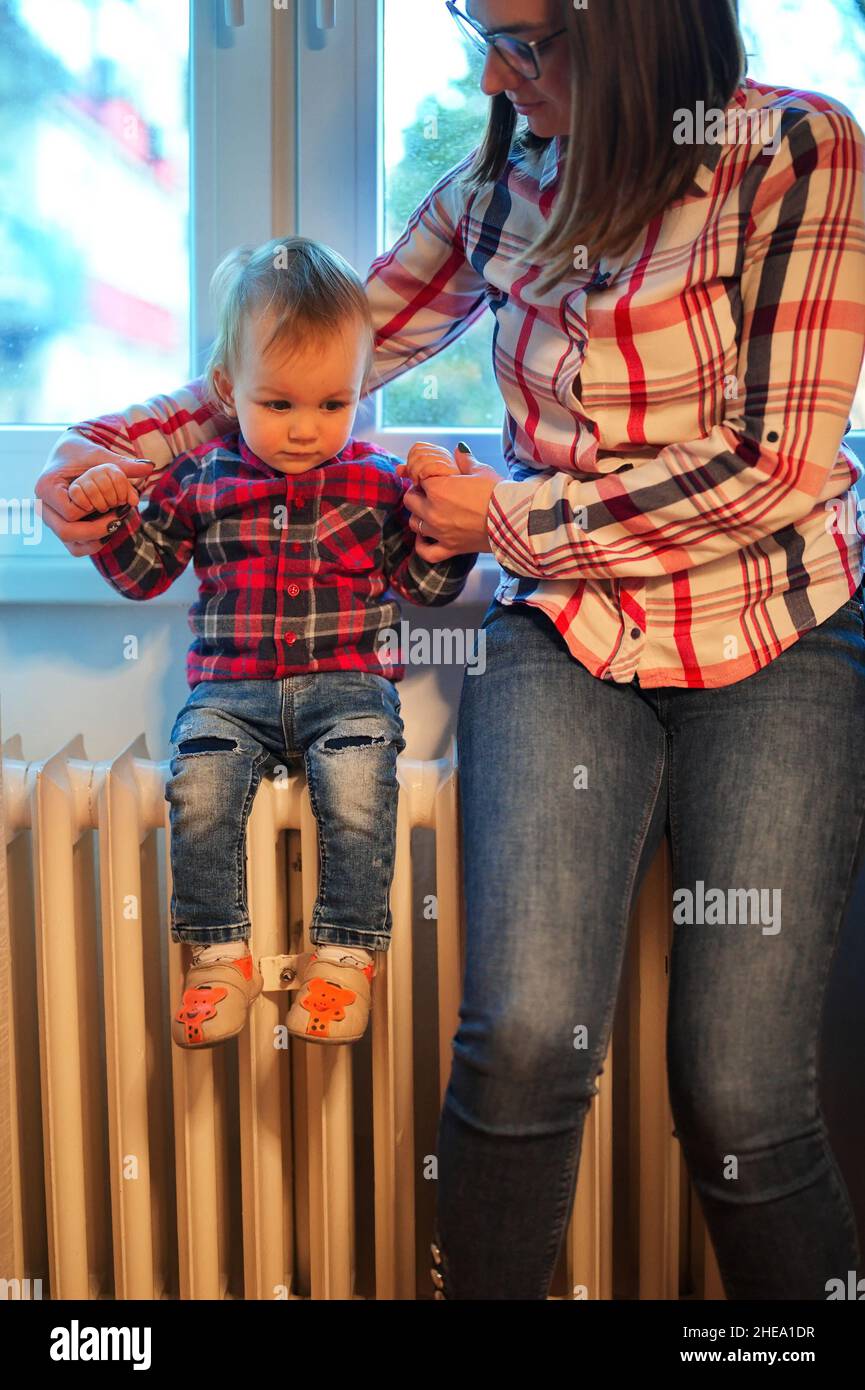 Cute little boy and his mother sitting on a radiator against the window ...