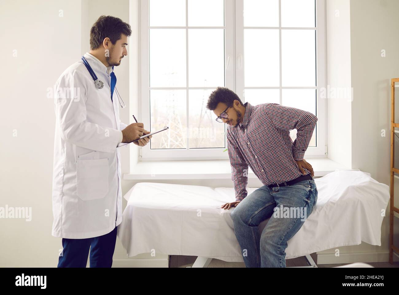 Young male patient complains to doctor of severe back pain during visit ...
