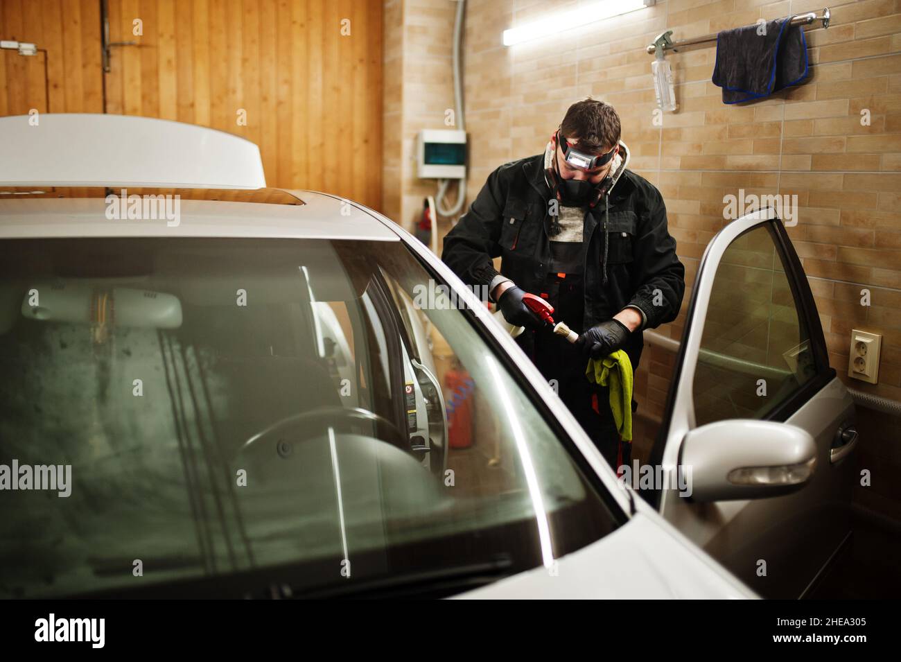 Man in uniform and respirator, worker of car wash center, cleaning car ...