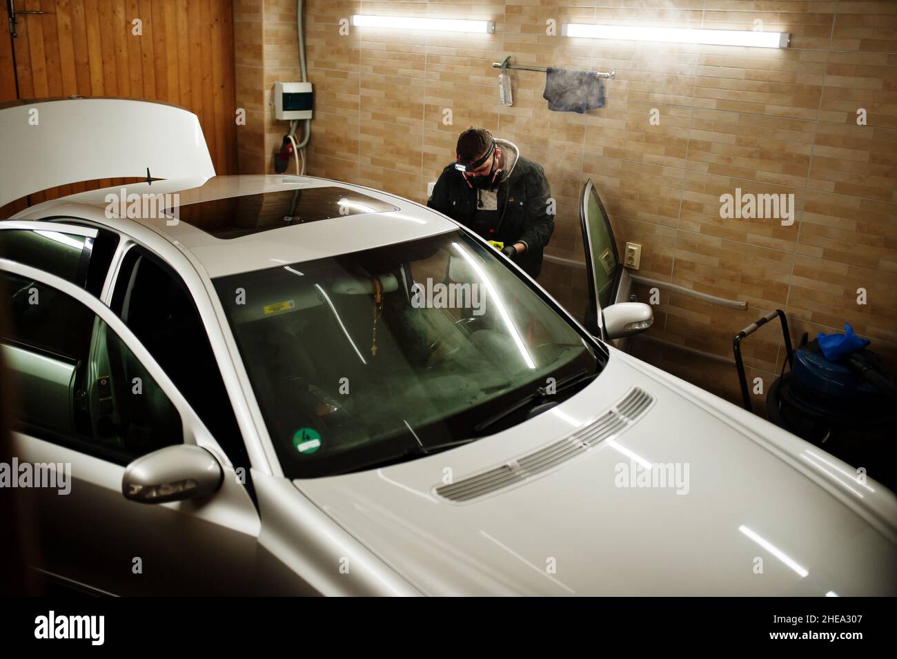 Man in uniform and respirator, worker of car wash center, cleaning car ...