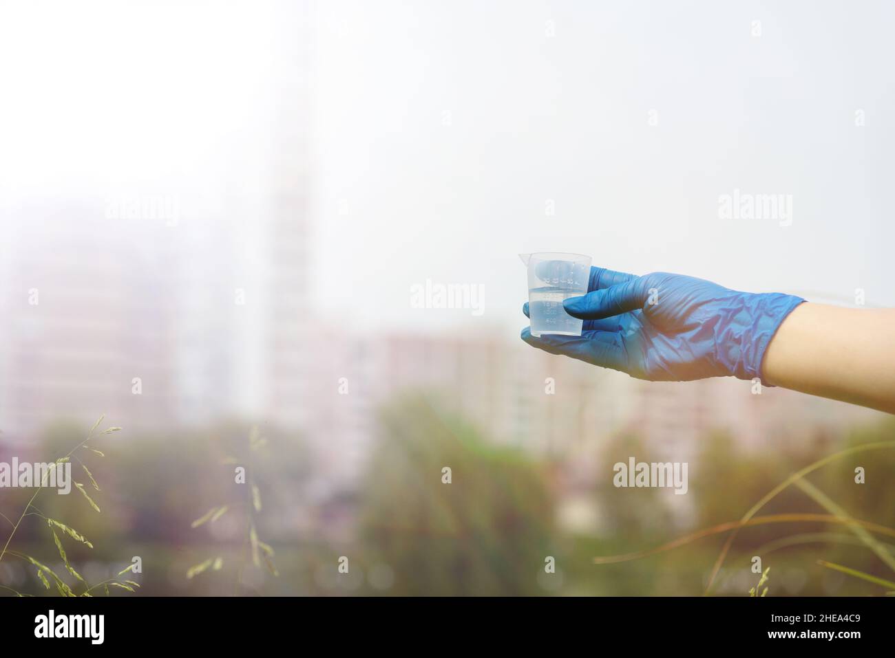 A gloved hand holds a beaker with a sample of water. Sampling from open ...