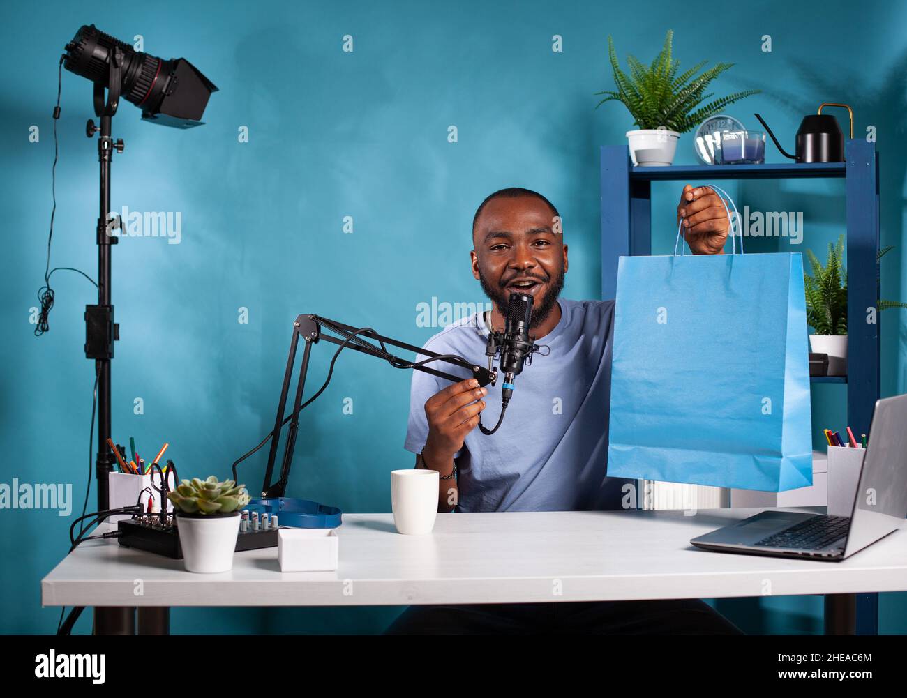 Vlogger holding boom arm microphone presenting giveaway blue paper gift ...