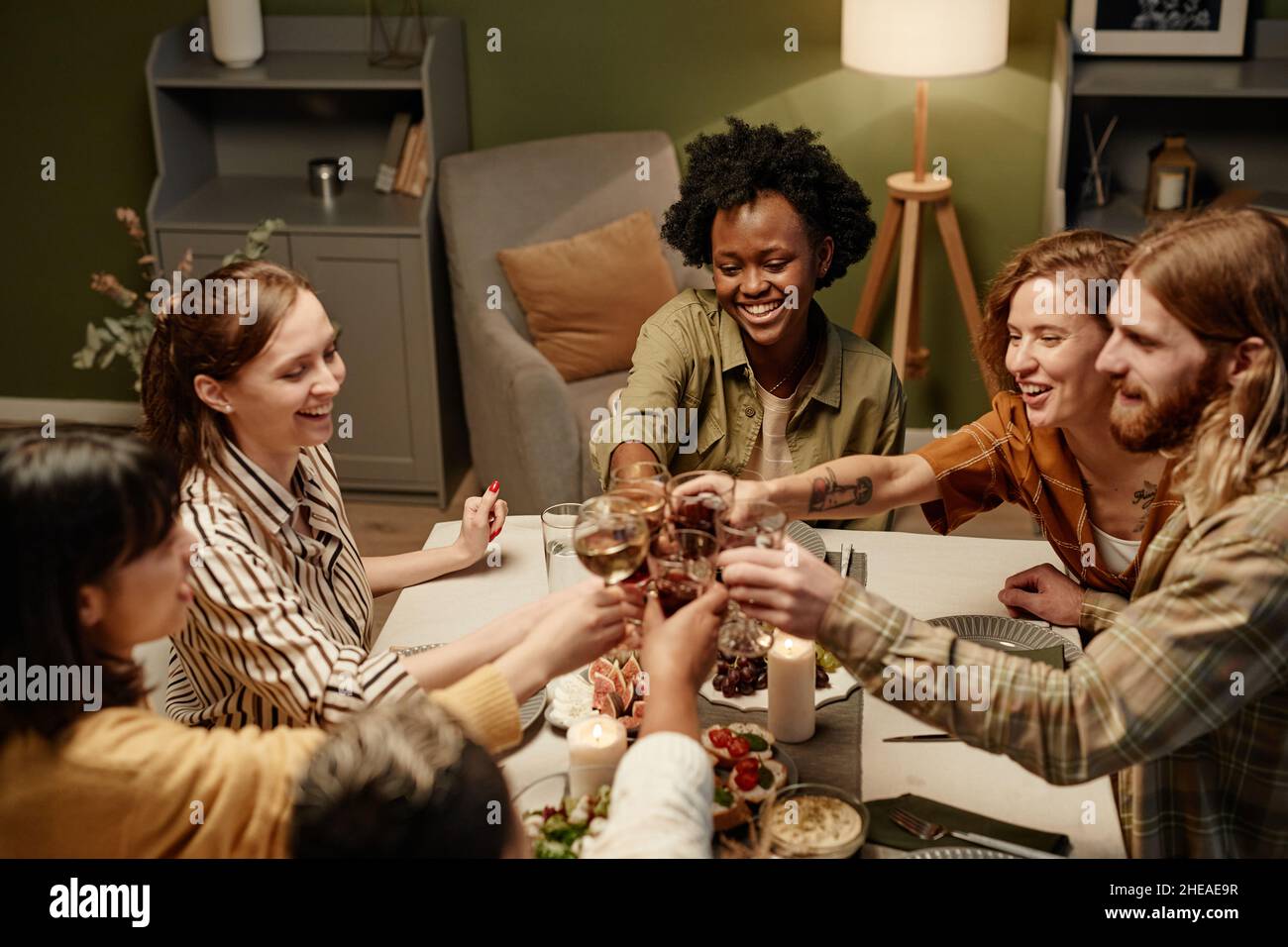 Group of happy friends toasting with drinks at dining table while ...