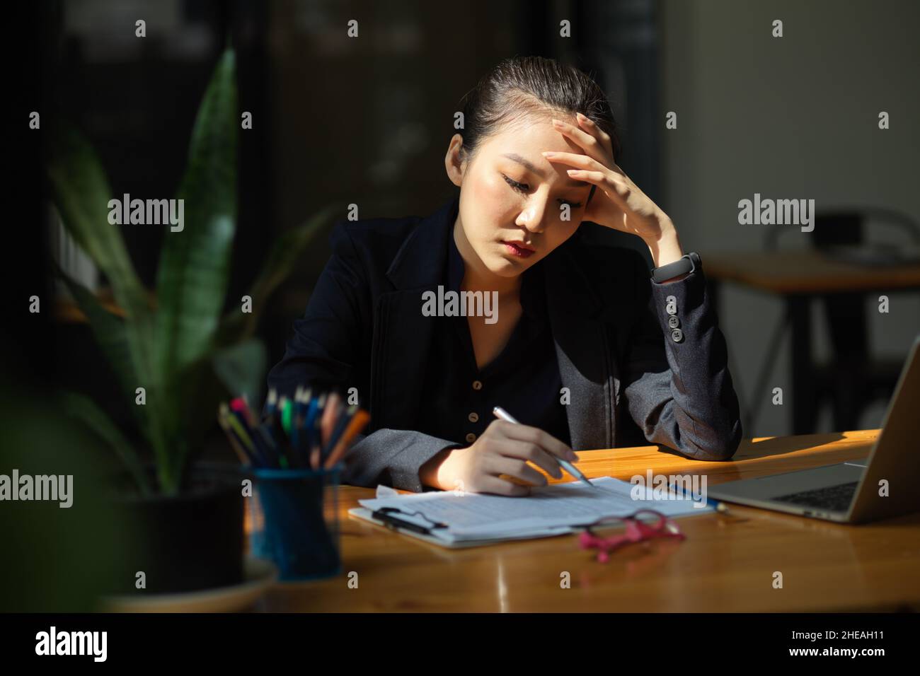 Tired Asian young business woman sitting at her desk and working on her ...