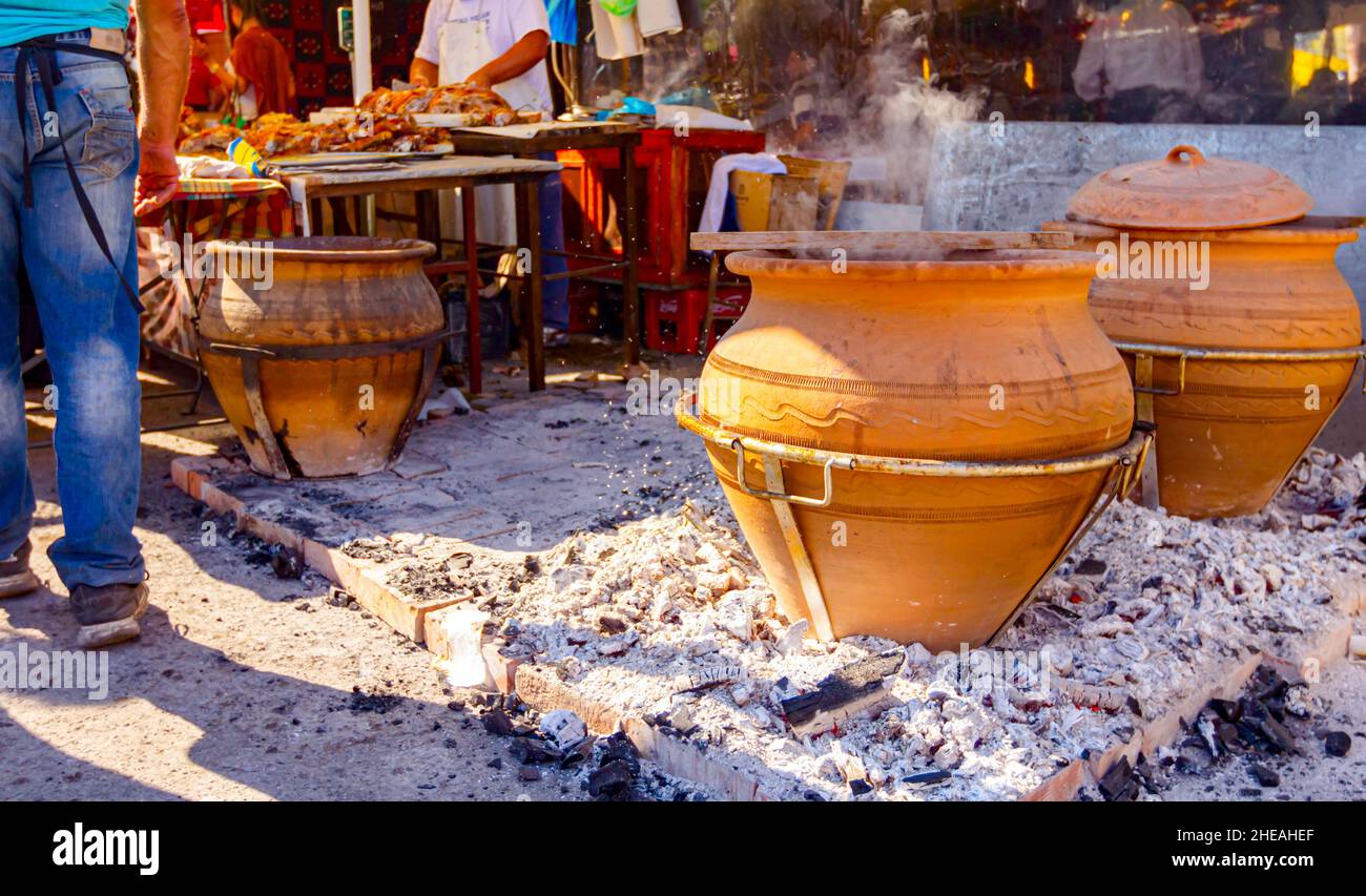 Big amount of food is cooking in a large ceramic, clay pots on embers ...