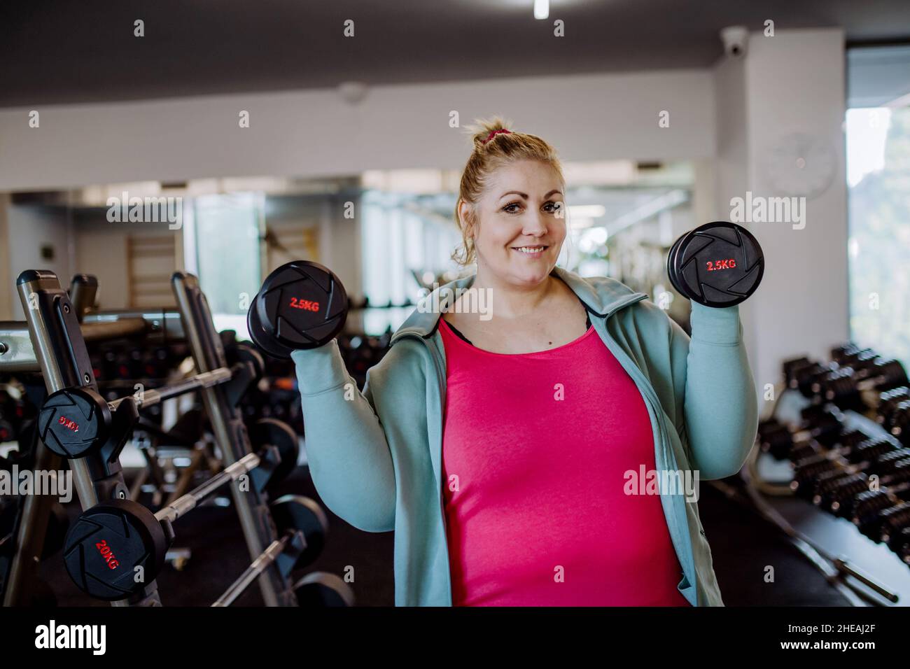 Plus size woman training and lifting dumbbells indoors in gym, looking ...