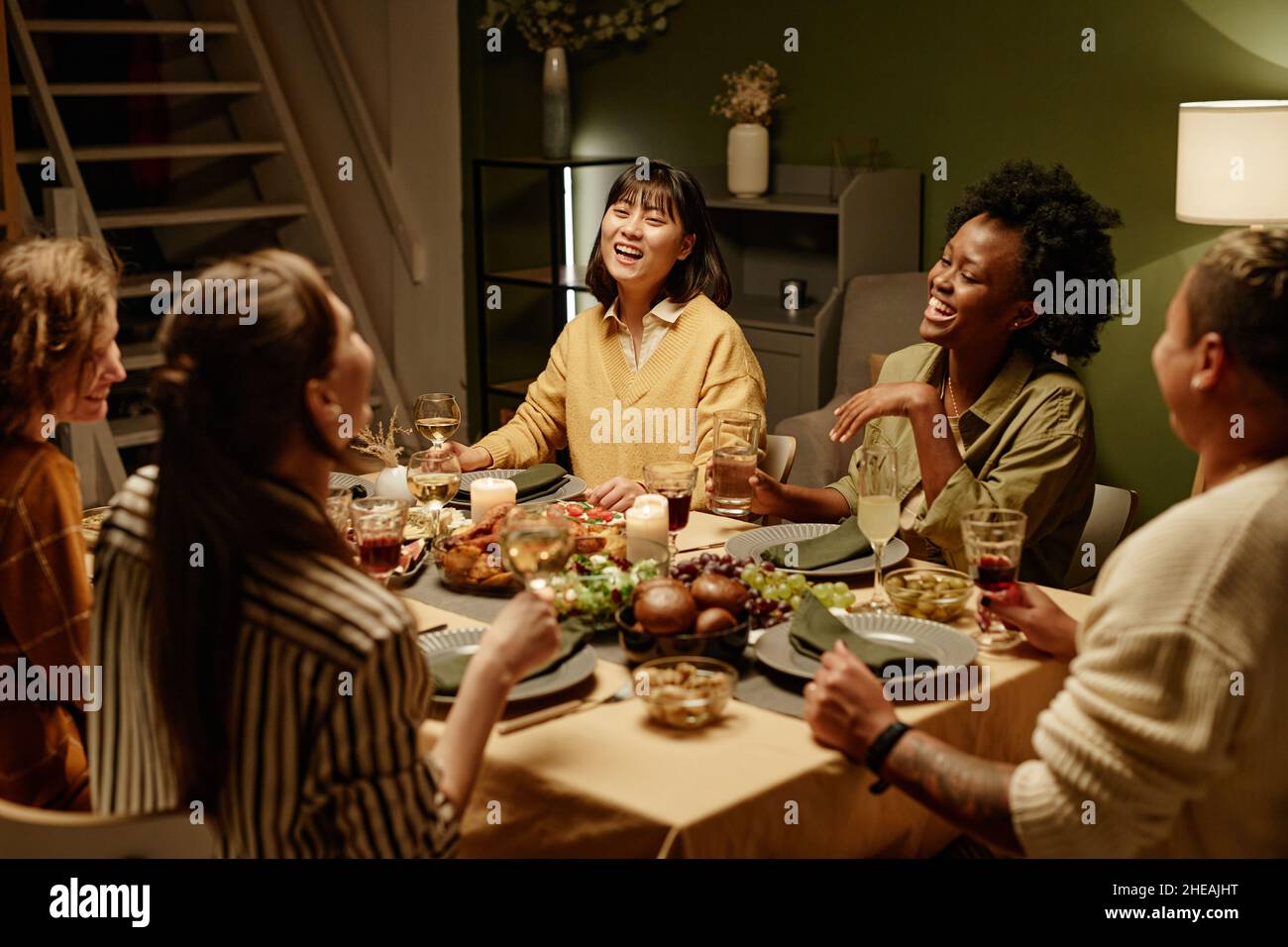 Group of young women laughing at the table during dinner party at home ...