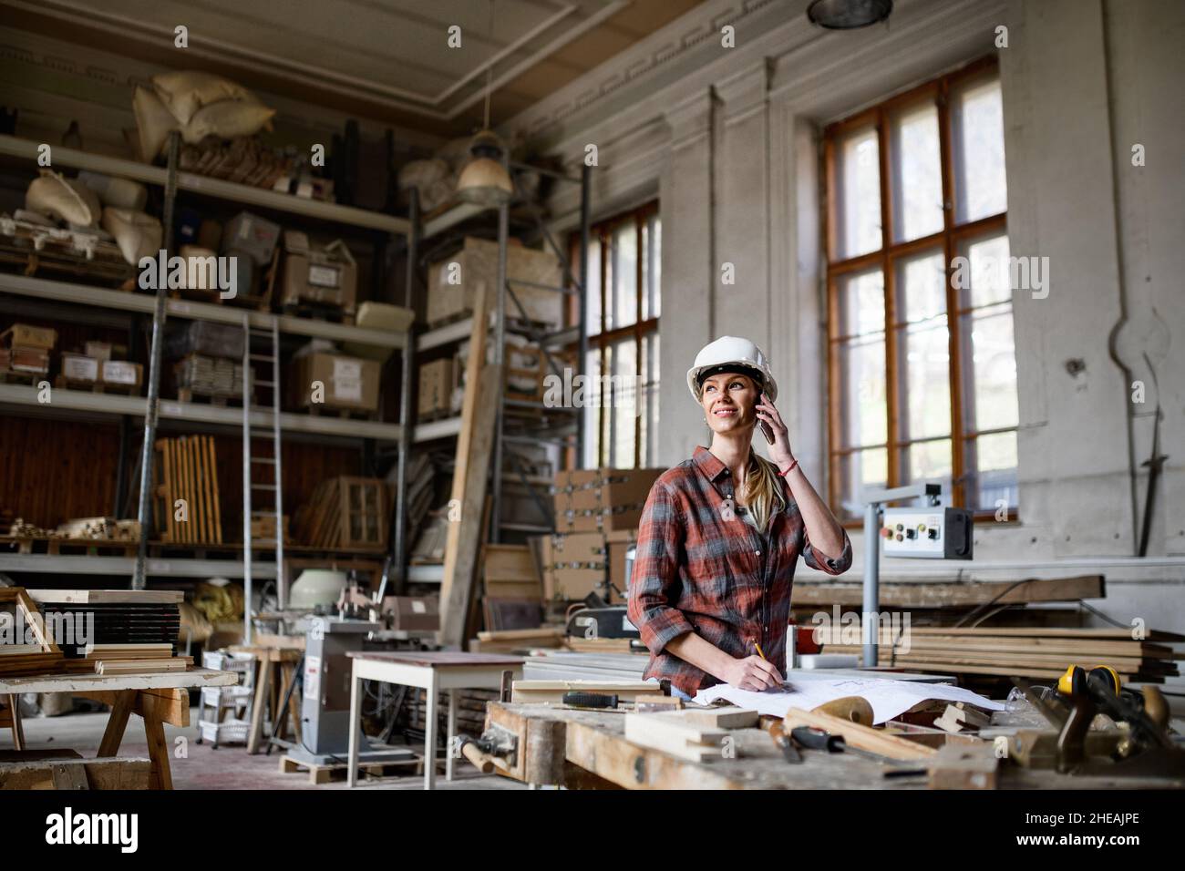 Female engineer holding blueprints and making phone call indoors in ...