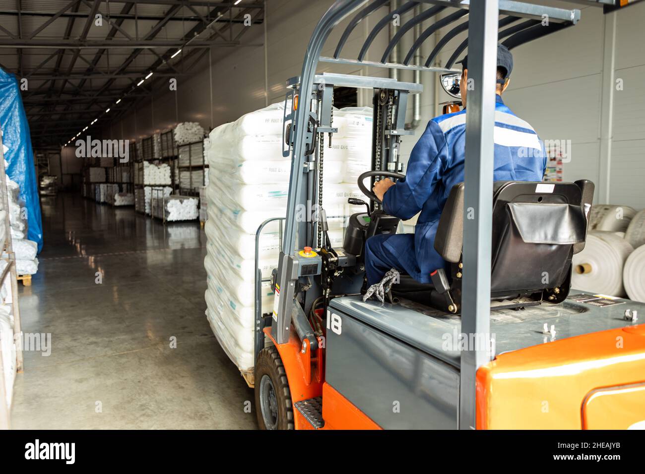 A man on a forklift works in a large warehouse, unloads bags of raw ...